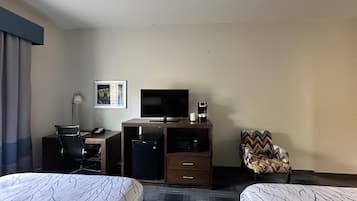 Quarto de hotel com duas camas, uma escrivaninha com televisão, um café e uma poltrona estampada.