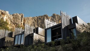 Um edifício moderno com vários quartos, janelas amplas e um penhasco rochoso ao fundo.