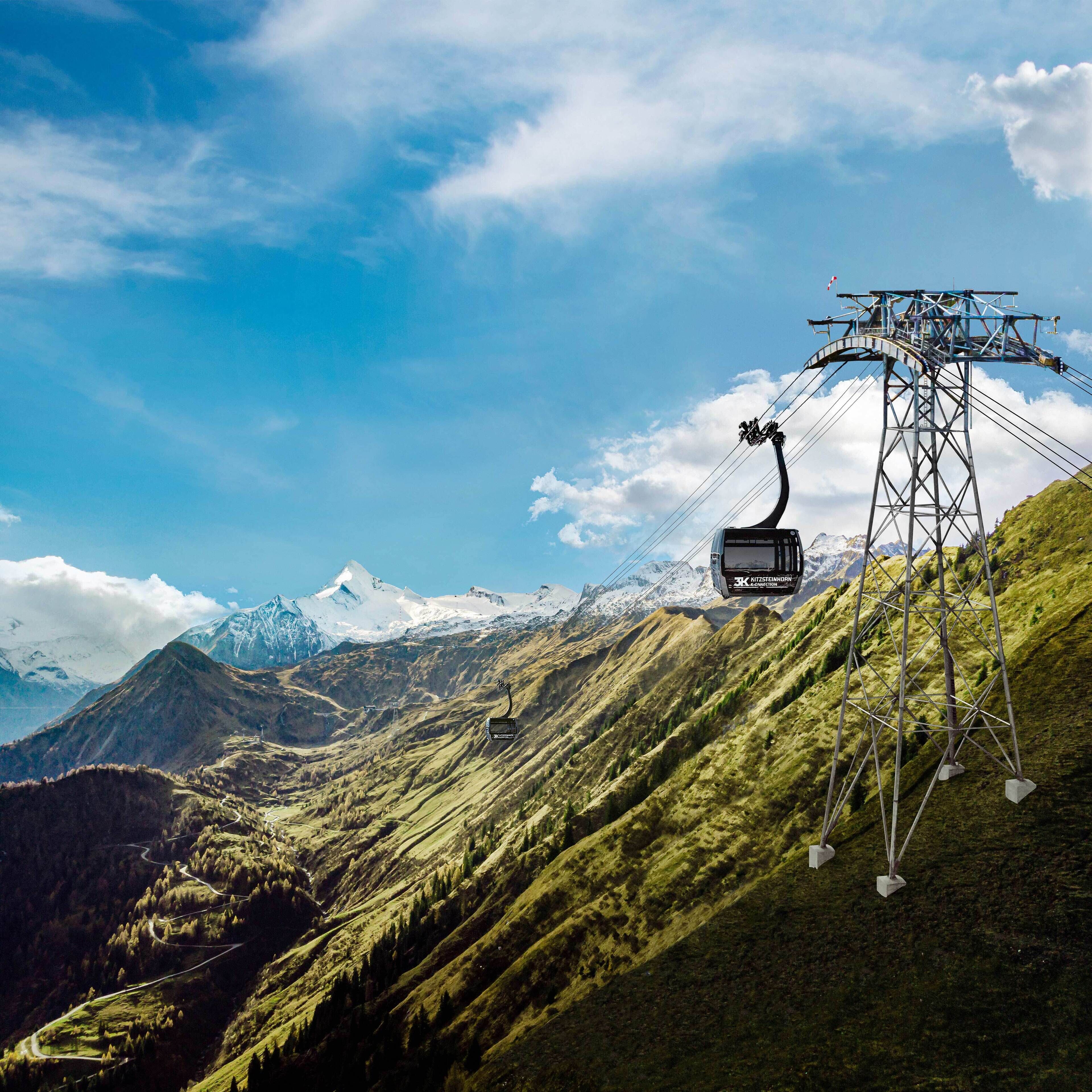 Um sistema de teleférico com paisagem montanhosa ao fundo, incluindo picos nevados e céu claro.