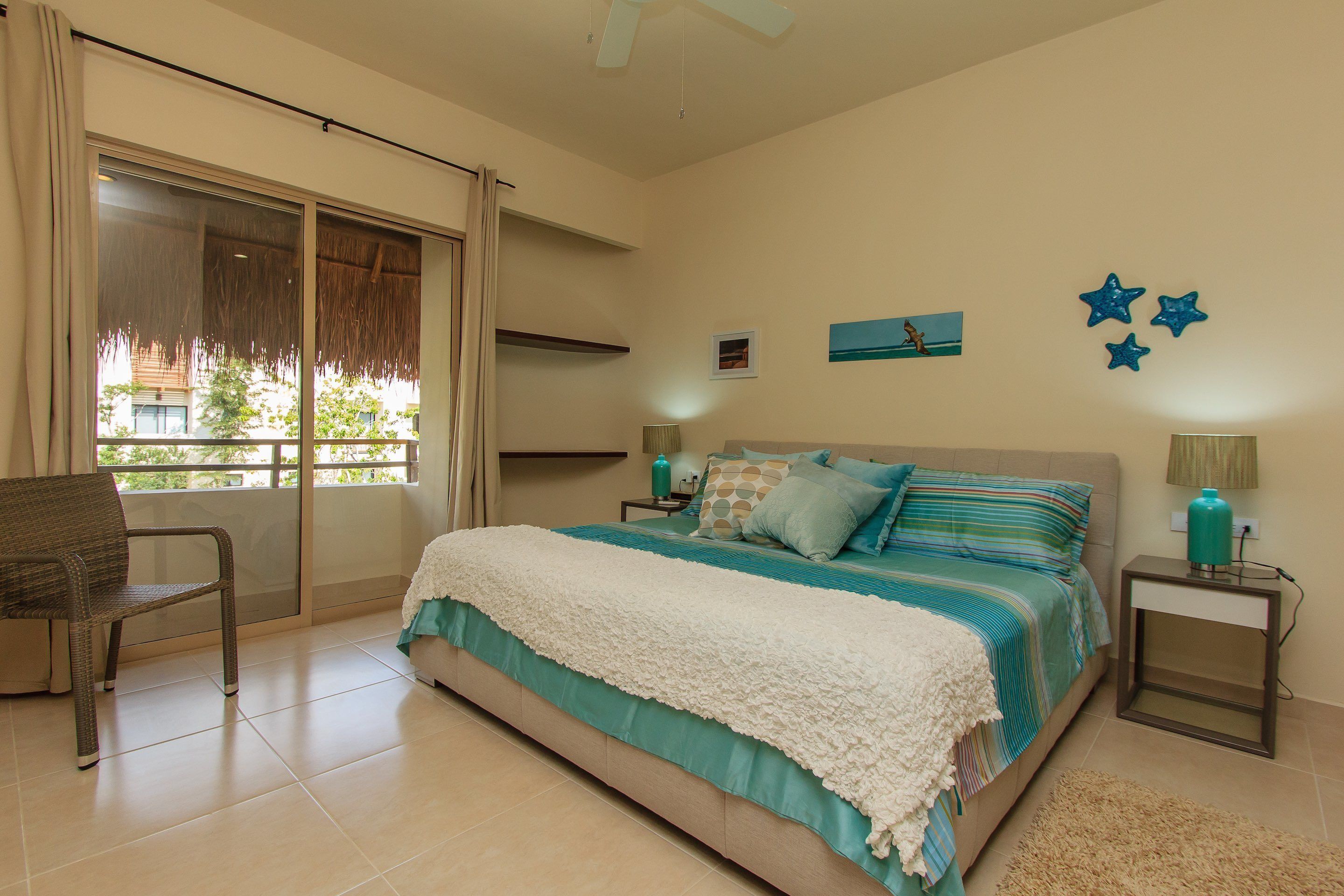 Quarto com cama, cadeira, mesa de cabeceira, abajur e janela com cortinas.