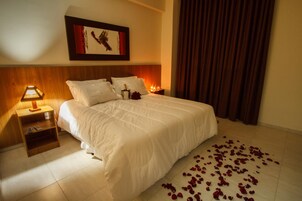 Uma cama bem arrumada com roupa de cama branca, um abajur e um quadro na parede.