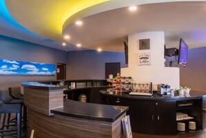Uma área de bar moderna com balcão curvo, espaço para café e uma TV na parede.