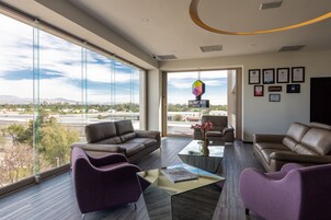 Um lobby de hotel moderno com sofás de couro, uma mesa de centro de vidro e grandes janelas com vista para a cidade.