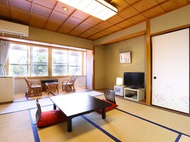 Quarto japonês tradicional com tatames, uma mesa baixa, cadeiras, televisão e uma porta de correr.