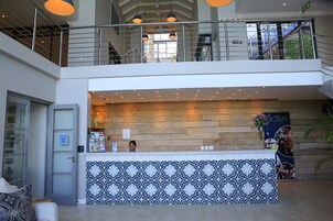 Uma área de recepção com parede de azulejos estampados, um recepcionista e uma escadaria que leva a um andar superior.
