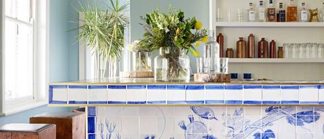 Uma cozinha com revestimento de azulejos azul e branco, uma janela com moldura branca e uma prateleira com garrafas e copos.
