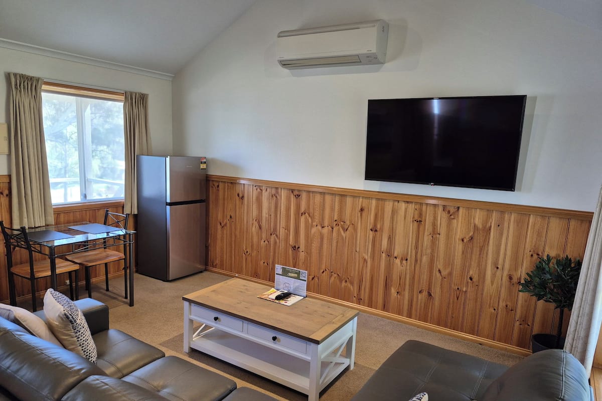 Um espaço de estar compacto com sofá, mesa de jantar, geladeira, TV e painel de parede de madeira.