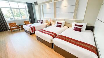 Quarto de hotel com duas camas, uma cadeira de madeira, uma mesinha e uma janela com cortinas.