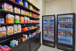 Um corredor de supermercado com prateleiras repletas de diversos produtos alimentícios e dois refrigeradores de bebidas.