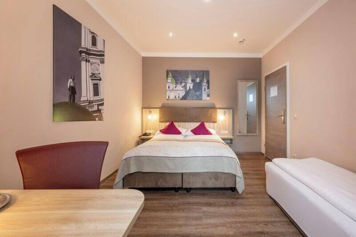Quarto de hotel com cama, mesas de cabeceira, uma cadeira e obras de arte nas paredes.