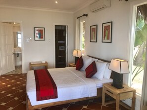 Quarto de hotel com uma cama grande, duas mesas de cabeceira com luminárias, um guarda-roupa e um banheiro visível através de uma porta aberta.