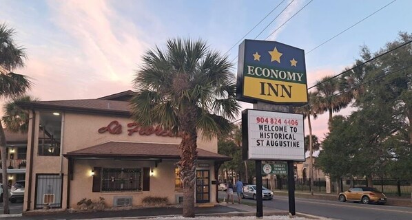 Um edifício de dois andares com uma placa indicando 'Economy Inn' e um letreiro de boas-vindas para 'Historical St Augustine'.