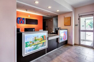 Uma área de recepção de hotel com um painel de exibição digital, uma placa indicando o número 6 e uma saída.