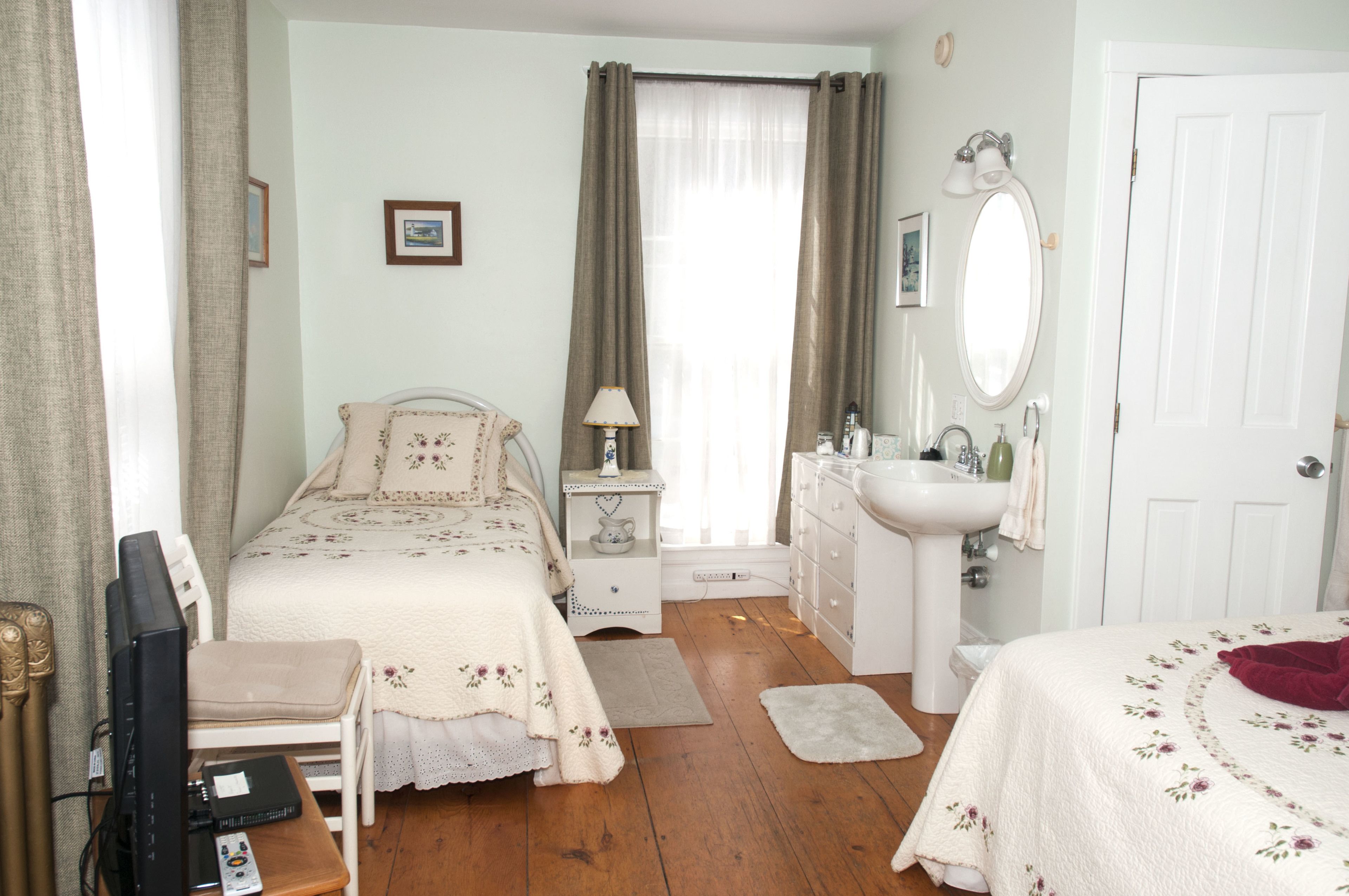 Quarto com cama, mesa de cabeceira, luminária, cômoda, espelho e porta.