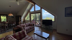 Uma sala de estar ampla, com uma grande janela, um ventilador de teto e uma televisão.