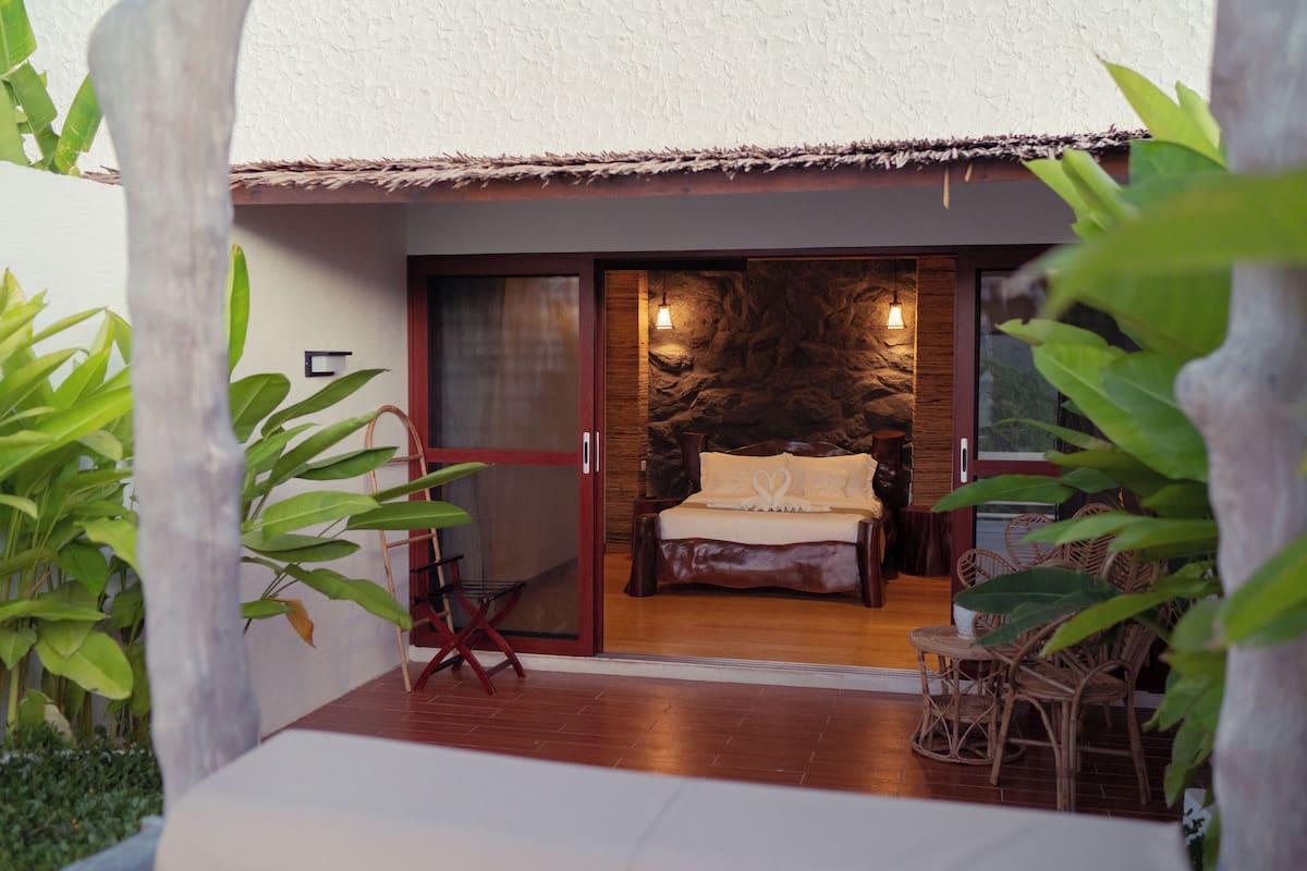 Quarto com parede de pedra, uma cama e um pequeno espaço de estar com cadeiras.