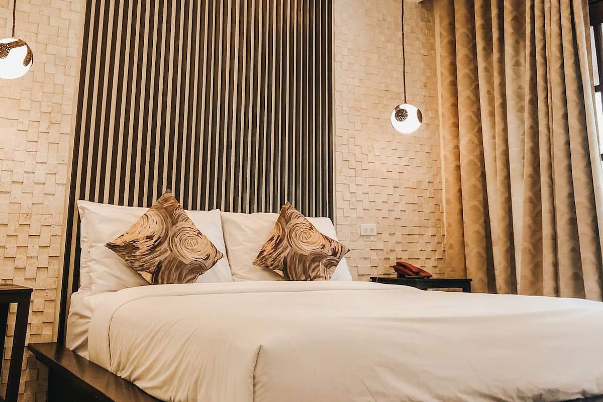 Quarto moderno com parede em tijolos, cabeceira de ripas e uma cama grande com roupa de cama branca e almofadas decorativas.