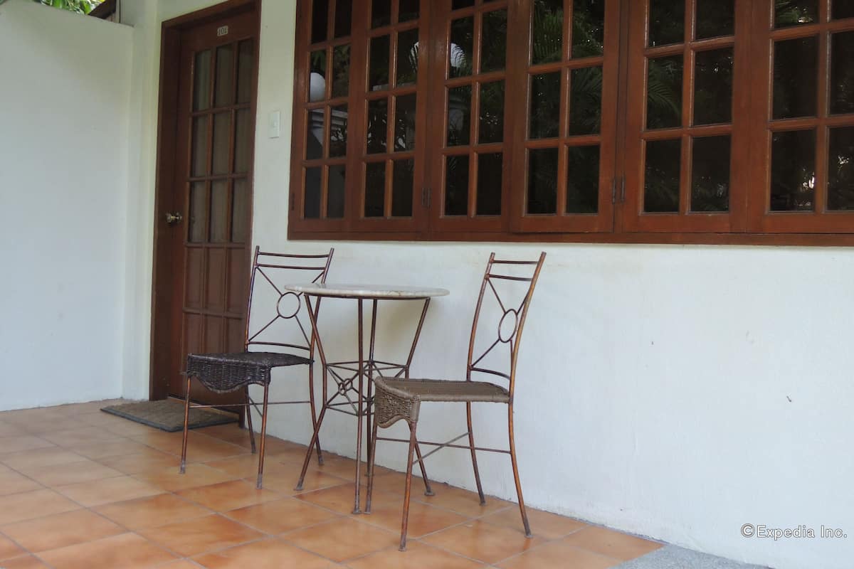 Um pátio com mesa e duas cadeiras, uma porta de madeira e uma janela com vários painéis.