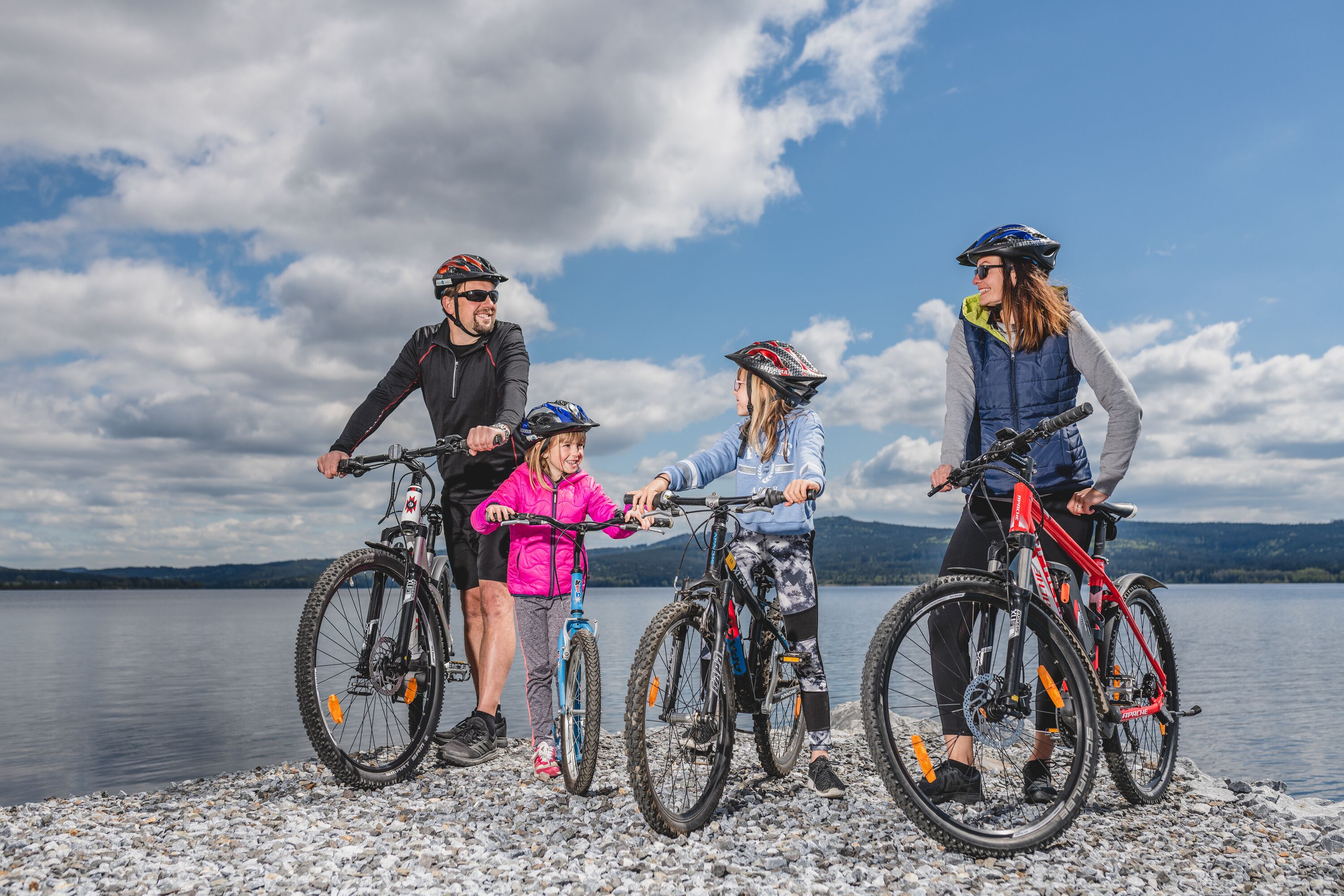 Um grupo de pessoas em bicicletas à beira de um lago, com céu limpo.