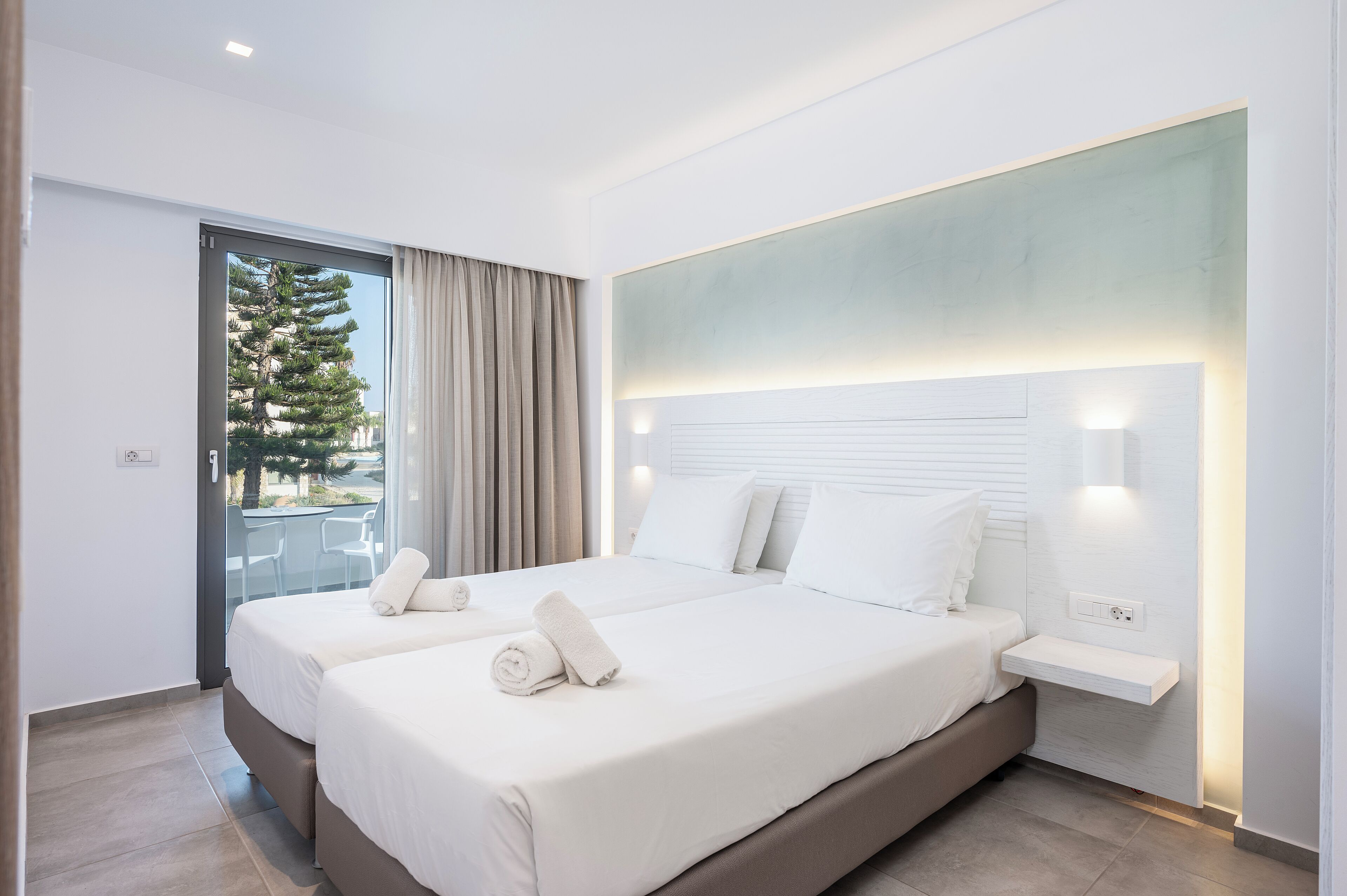 Quarto de hotel moderno com duas camas, varanda e vista para árvores.
