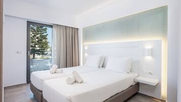 Quarto de hotel moderno com duas camas, varanda e vista para árvores.