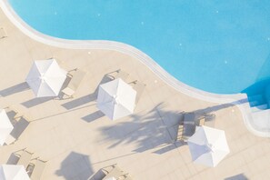 Vista aérea de uma área de piscina com guarda-sóis brancos e espreguiçadeiras dispostas ao redor.