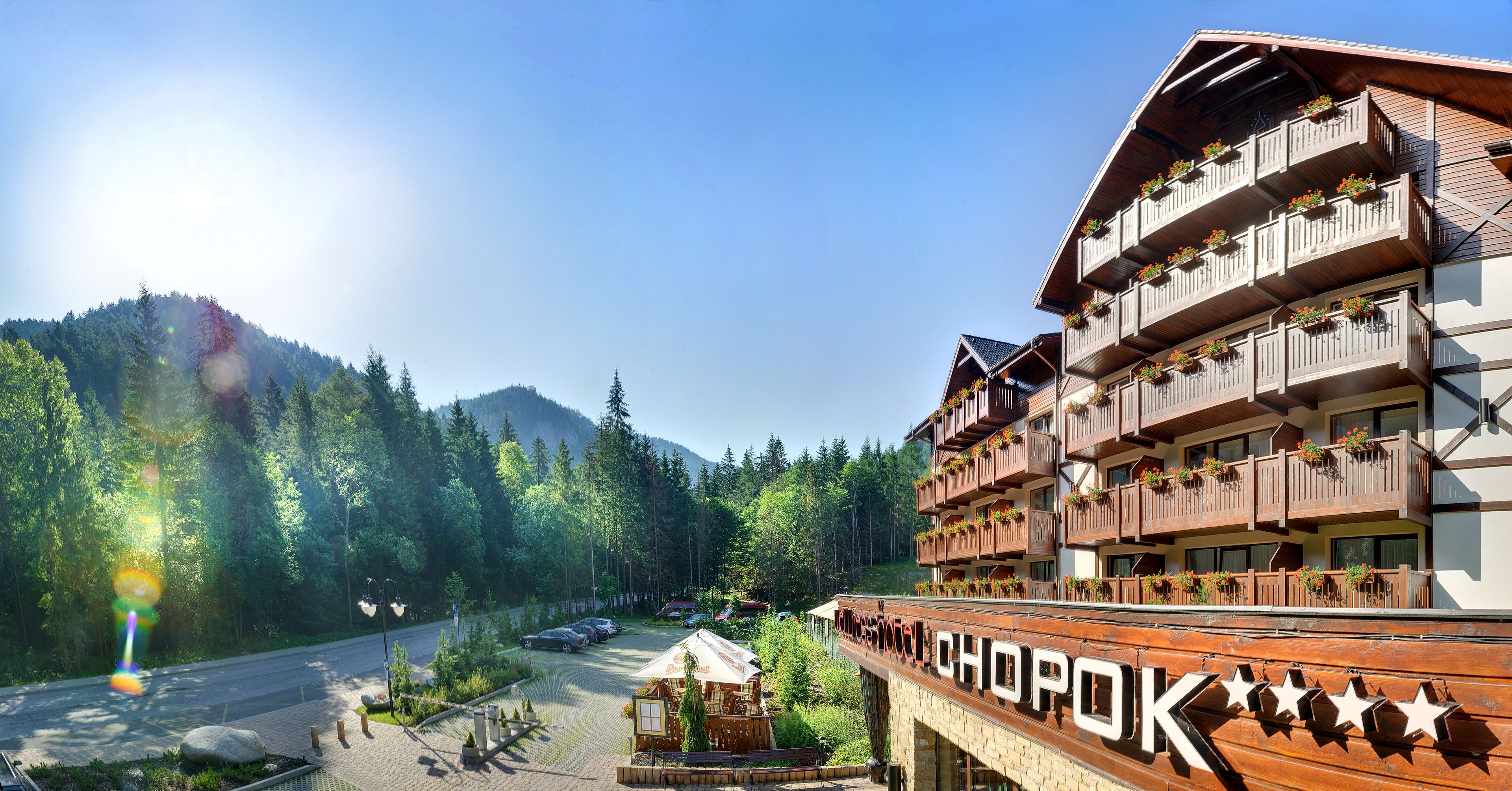 Um hotel com várias varandas decoradas com floreiras, vista desobstruída da floresta circundante e uma montanha ao fundo.