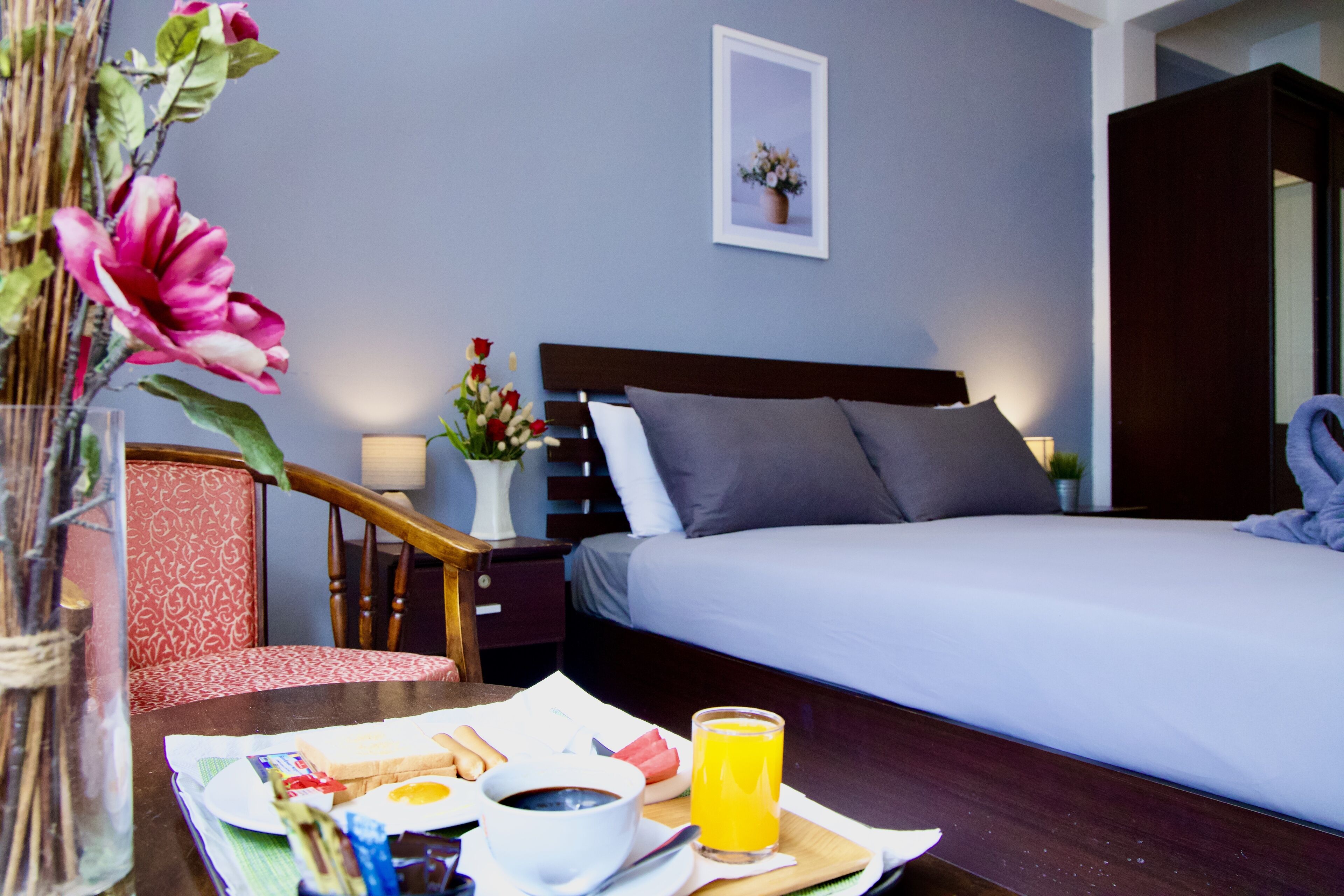 Quarto de hotel com cama, mesa de cabeceira e bandeja de café da manhã com ovos, torradas, café e suco de laranja.