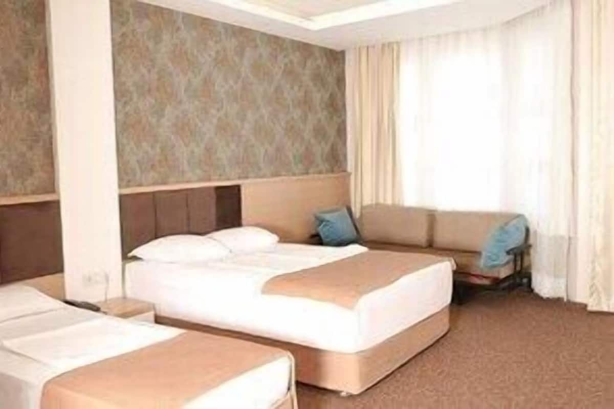 Quarto de hotel com duas camas, um sofá e uma janela com cortinas.
