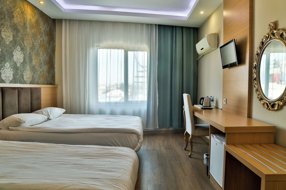 Quarto de hotel com duas camas, uma escrivaninha, um espelho, uma televisão e uma janela com cortinas.