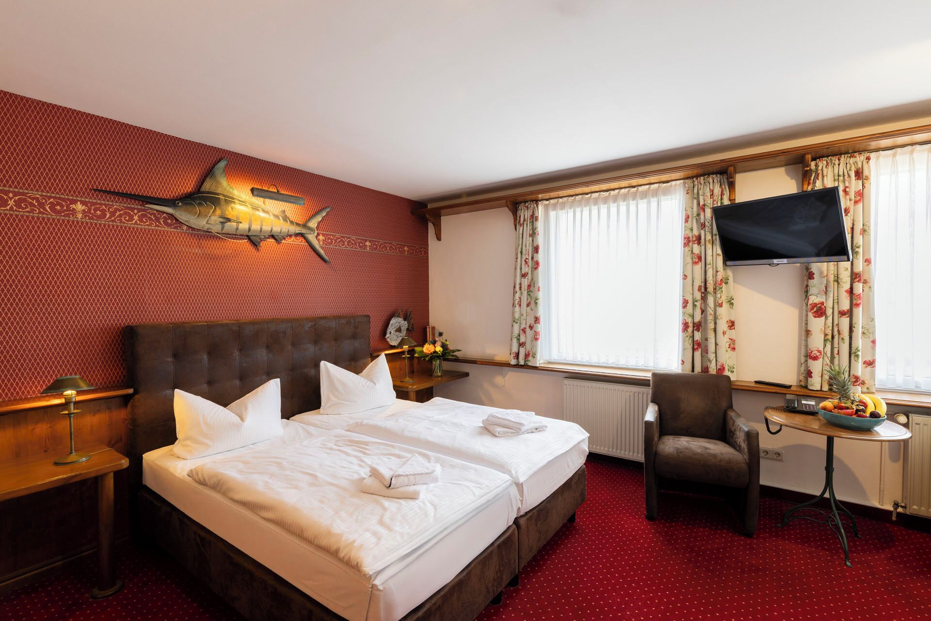 Quarto de hotel com uma cama grande, uma mesa com cadeira, uma televisão e um peixe decorativo na parede.
