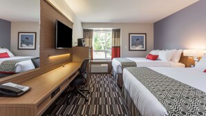 Quarto de hotel com duas camas, uma escrivaninha, uma cadeira, uma televisão e uma janela com cortinas.