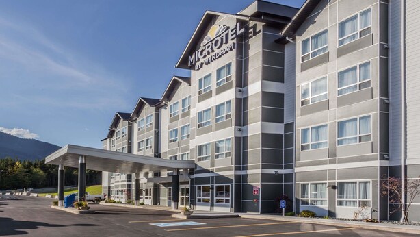 Um hotel Microtel moderno com estrutura em dois andares, área de estacionamento coberta e montanhas ao fundo.