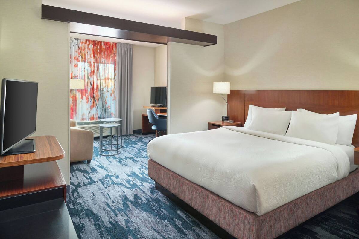 Quarto de hotel com uma cama grande, uma escrivaninha, uma televisão e uma cadeira.