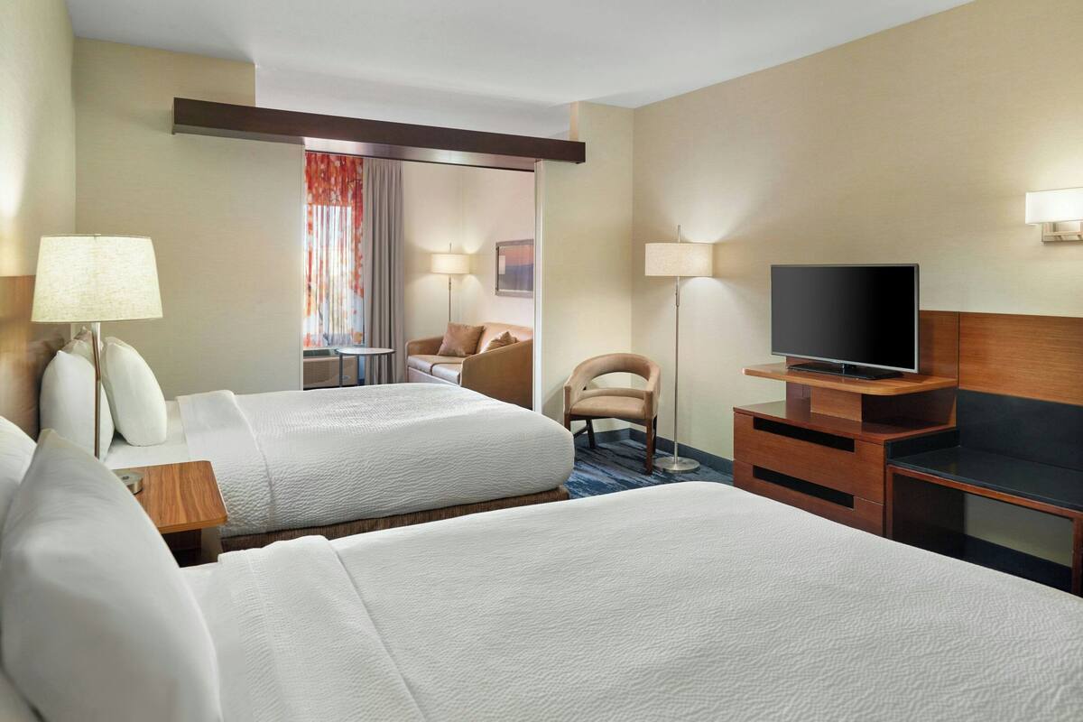 Quarto de hotel com duas camas, televisão, escrivaninha e uma cadeira.