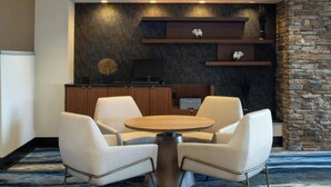 Uma área de refeições moderna com uma mesa redonda e quatro cadeiras, uma cozinha com TV de tela plana e uma parede de destaque em pedra.