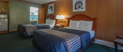 Quarto de hotel com duas camas, uma escrivaninha, uma cadeira, uma luminária e um frigorífico.
