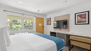 Quarto de hotel com cama, escrivaninha, televisão e janela com vista para o verde.