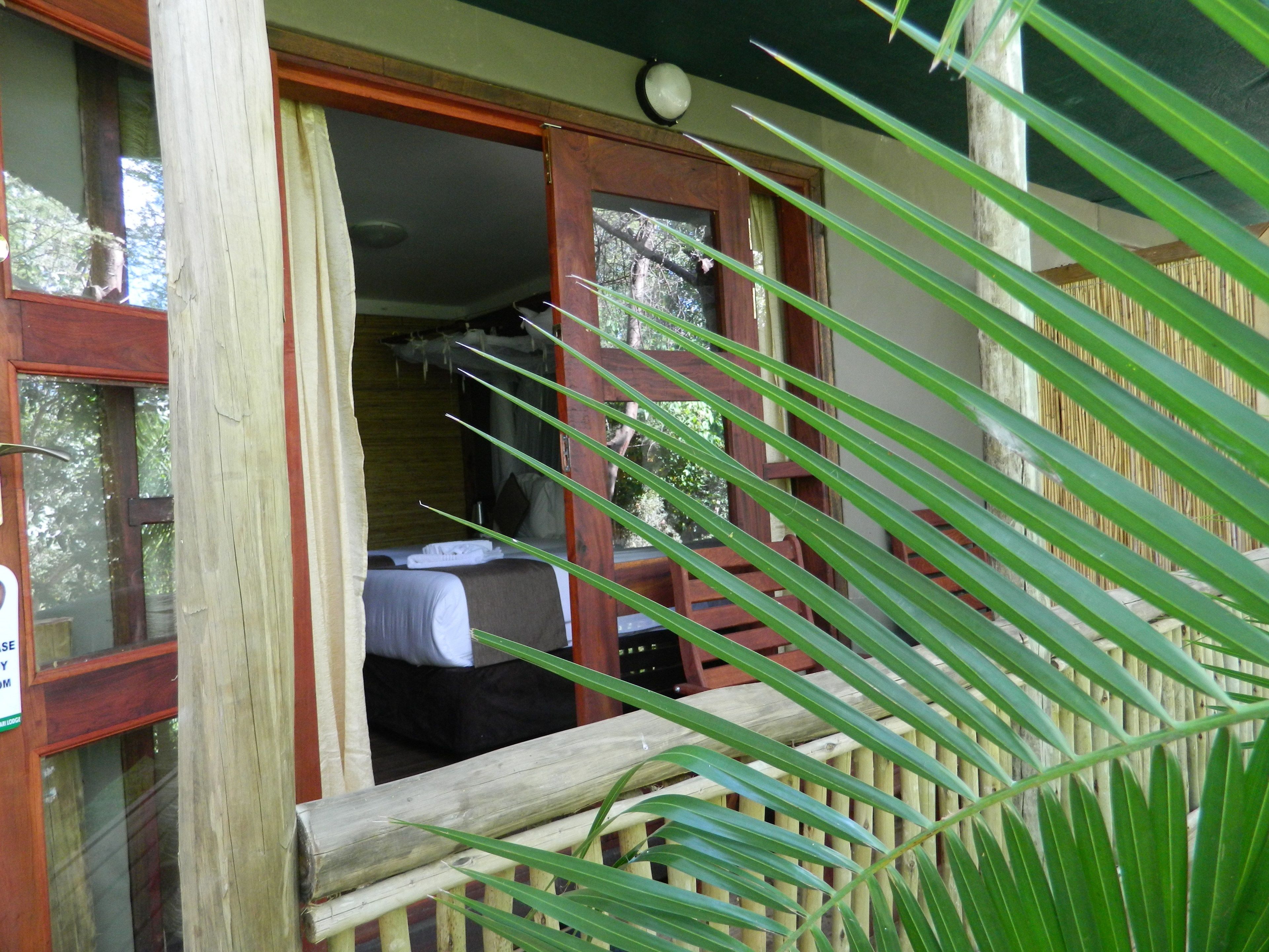 Uma porta de madeira que dá para um quarto com cama e janela.