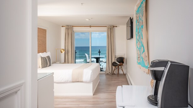 Quarto de hotel com cama, escrivaninha, cadeira, máquina de café, televisão e vista para o oceano.