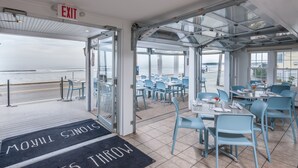 Restaurante com vista para o mar, mesas e cadeiras, e um sinal de saída.