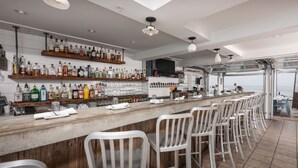 Um bar com um balcão comprido, várias prateleiras de garrafas e alguns taburetes brancos.