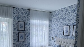 Um quarto com uma cama grande, cortinas brancas e papel de parede com padrão azul.
