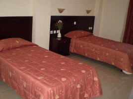 Quarto de hotel com duas camas de solteiro, uma mesa de cabeceira com um vaso e uma luminária na parede.