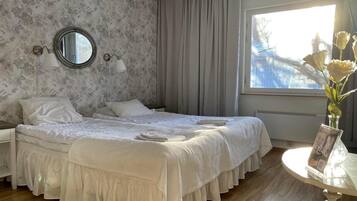 Quarto com cama, espelho redondo, mesa de cabeceira, janela com cortinas e um vaso com flores.