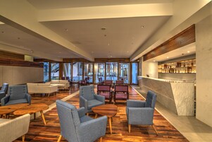 Um hall amplo com mobiliário moderno, área de bar e grandes janelas com vista.