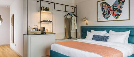 Quarto com cama, guarda-roupa, espelho, cabideiro e uma obra de arte na parede.