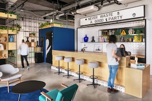 Uma área de bar moderna com banquetas, balcão e um letreiro com a frase 'NUNCA PERCA UMA BOA FESTA'.