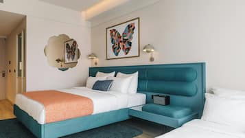 Quarto de hotel moderno com parede em tom de verde-água, cama com roupa de cama branca, pequena mesa de cabeceira e duas luminárias fixadas na parede.