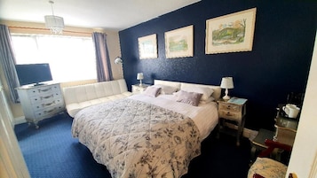 Quarto com cama, mesas de cabeceira, cômoda, televisão e obras de arte na parede.